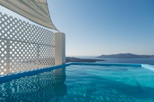 Uma piscina infinita com água azul cristalina, um muro treliçado branco e vista para o mar e montanhas ao longe.