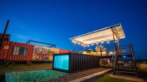 Uma casa container com um mural, um pequeno palco e uma estátua de pato amarelo.