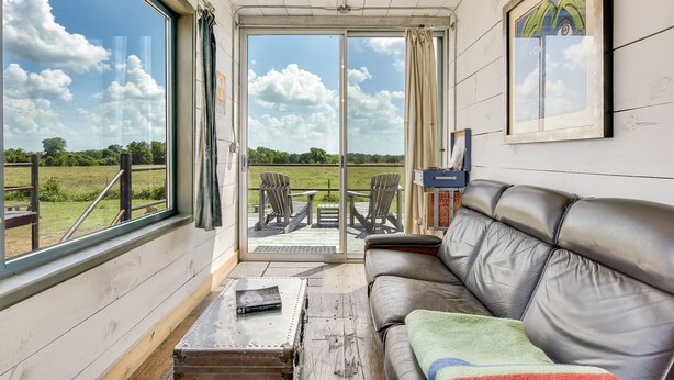 Quarto aconchegante com sofá de couro, uma mesa pequena e janela com vista para um campo gramado.