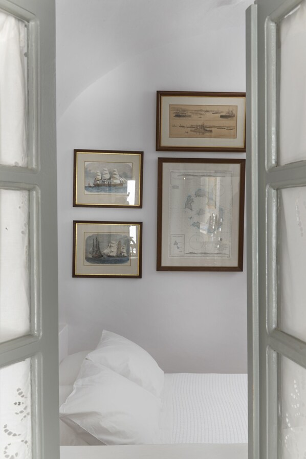 Quarto com cama, paredes brancas e três quadros na parede.