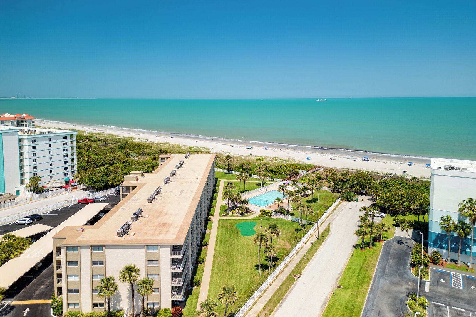 Um hotel com piscina no terraço, vista para a praia e estacionamento.