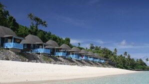 Um resort à beira-mar com bangalôs sobre a água, águas turquesa cristalinas e palmeiras.