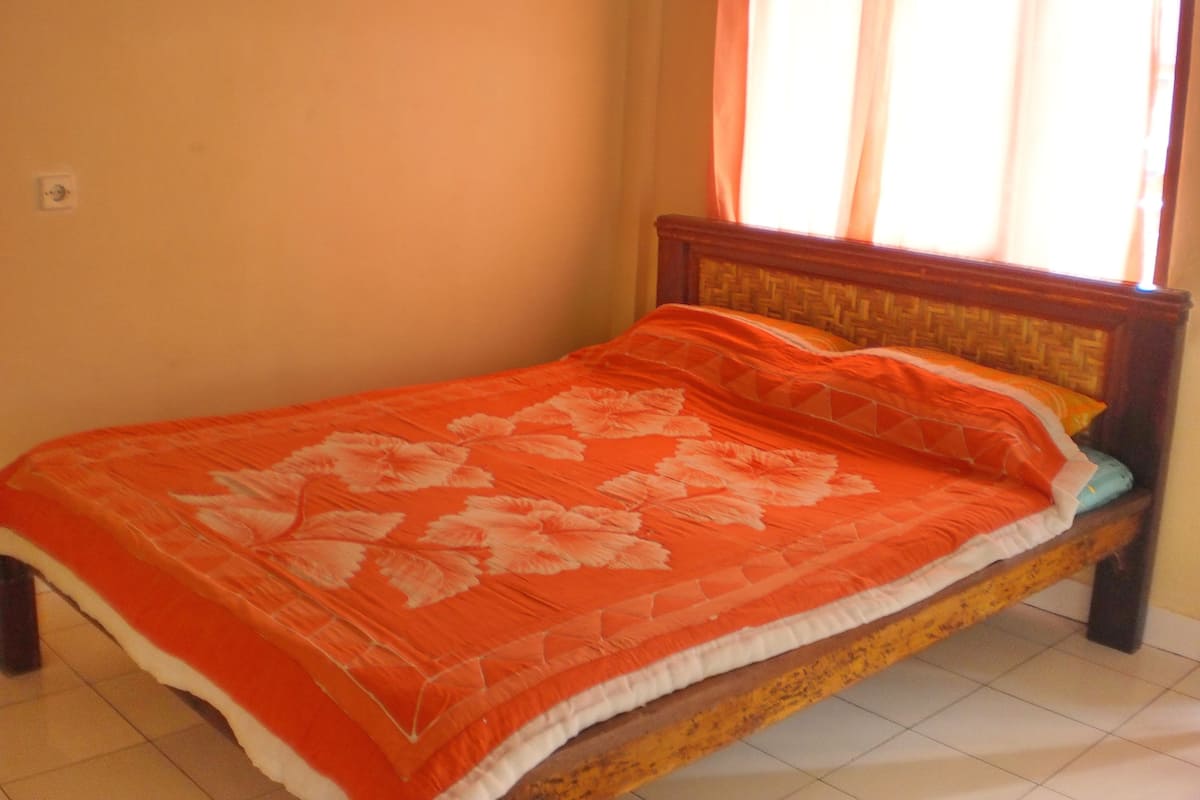 Uma cama com colcha estampada em flor, cabeceira de madeira e janela com cortinas.