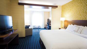 Quarto de hotel com uma cama grande, uma TV em suporte, uma mesa com cadeira e vista para o corredor.