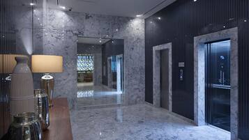 Um hall moderno com piso de mármore, balcão de recepção em madeira e um elevador.