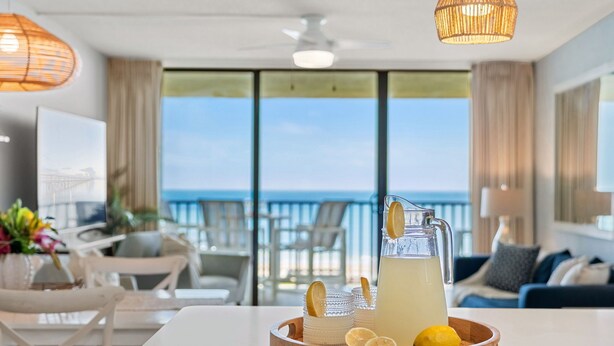 Uma área de refeições com uma mesa posta para dois, um jarro de limonada e uma bandeja de madeira com fatias de limão.