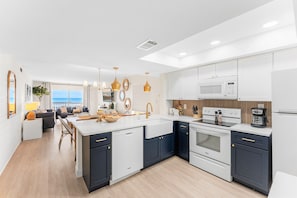 Uma cozinha moderna com armários brancos e escuros, uma ilha central e vista para o exterior.