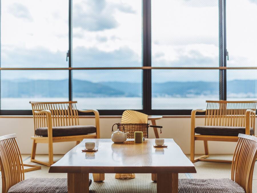 Quarto com uma grande janela, uma mesa de madeira e quatro cadeiras.