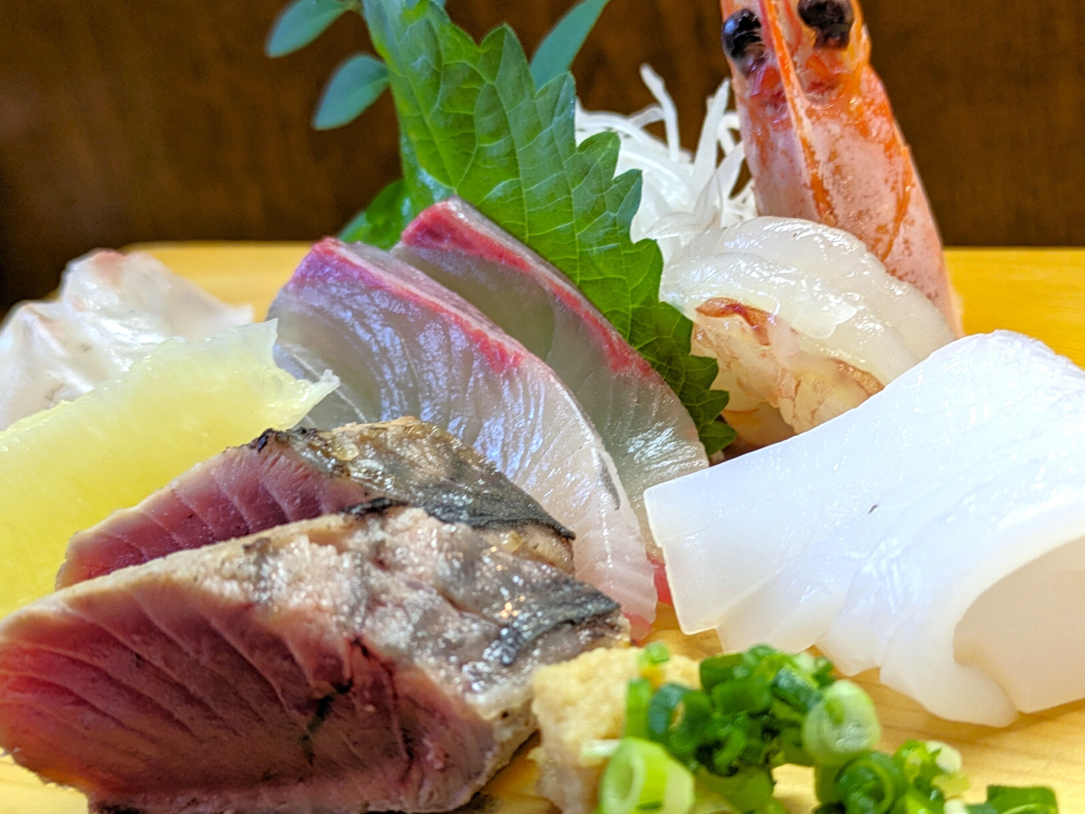 Variedade de frutos do mar, incluindo peixe, camarão e possivelmente sashimi, dispostos sobre uma mesa de madeira.