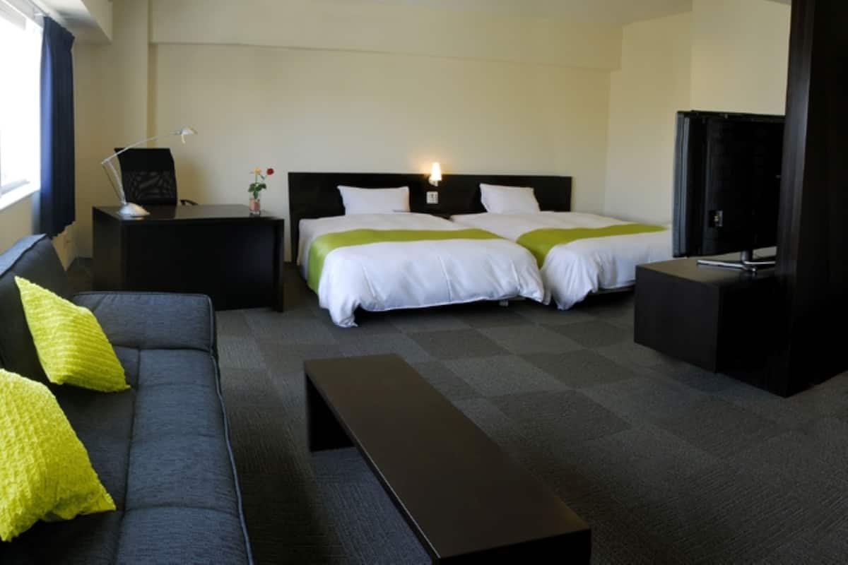 Quarto de hotel com duas camas, um sofá, uma TV e uma escrivaninha.