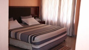 Uma cama de casal bem arrumada, com roupa de cama listrada, cabeceira e mesa de cabeceira com um vaso de flores.