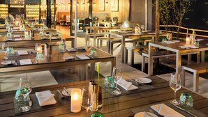 Um restaurante com várias mesas de madeira preparadas para refeições, cada uma com pratos, talheres e velas.