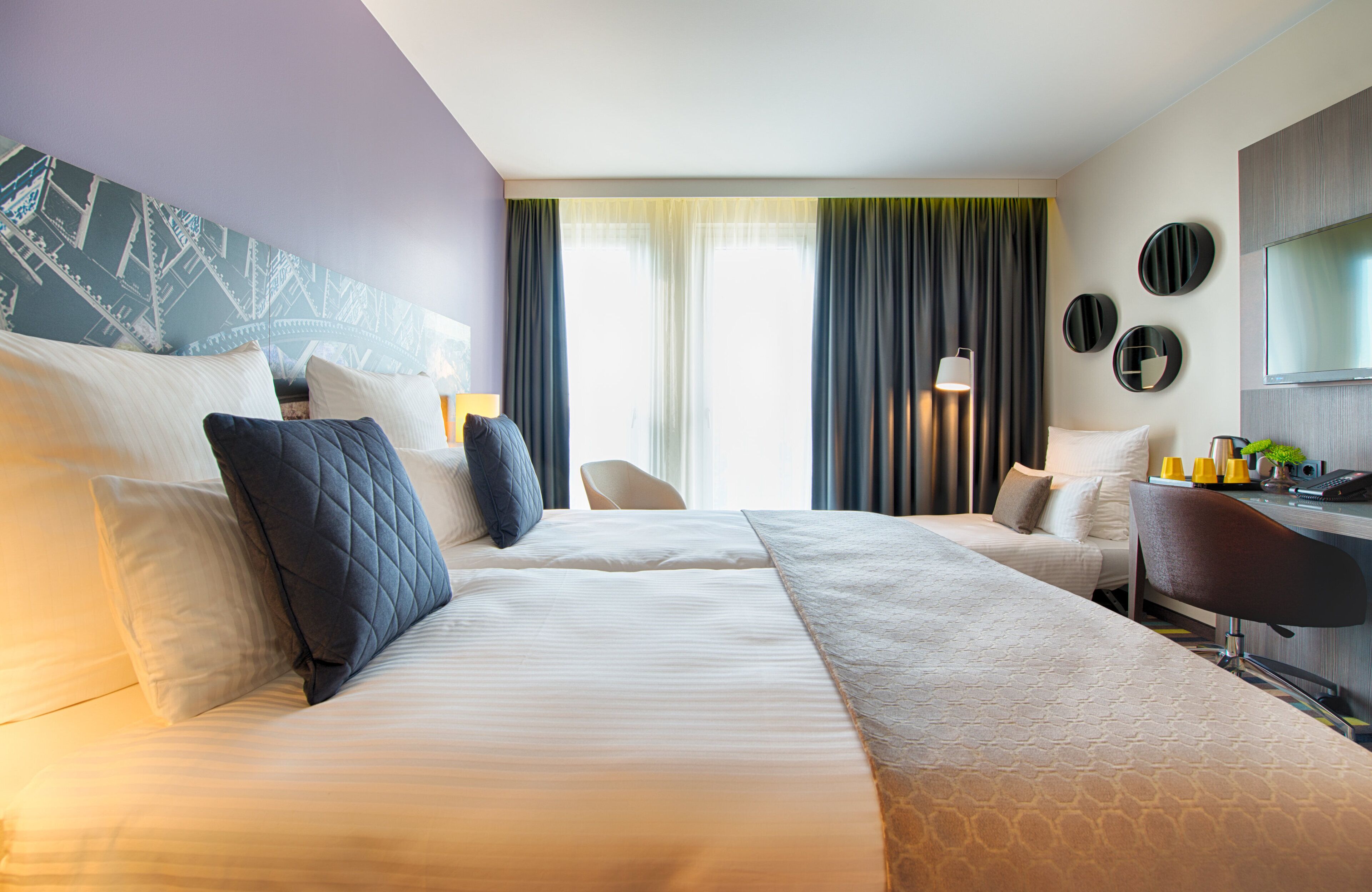 Quarto de hotel com uma cama grande, uma escrivaninha e uma televisão.