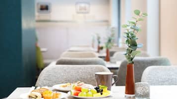 Uma mesa de café da manhã com pratos de doces, frutas e uma xícara de café.