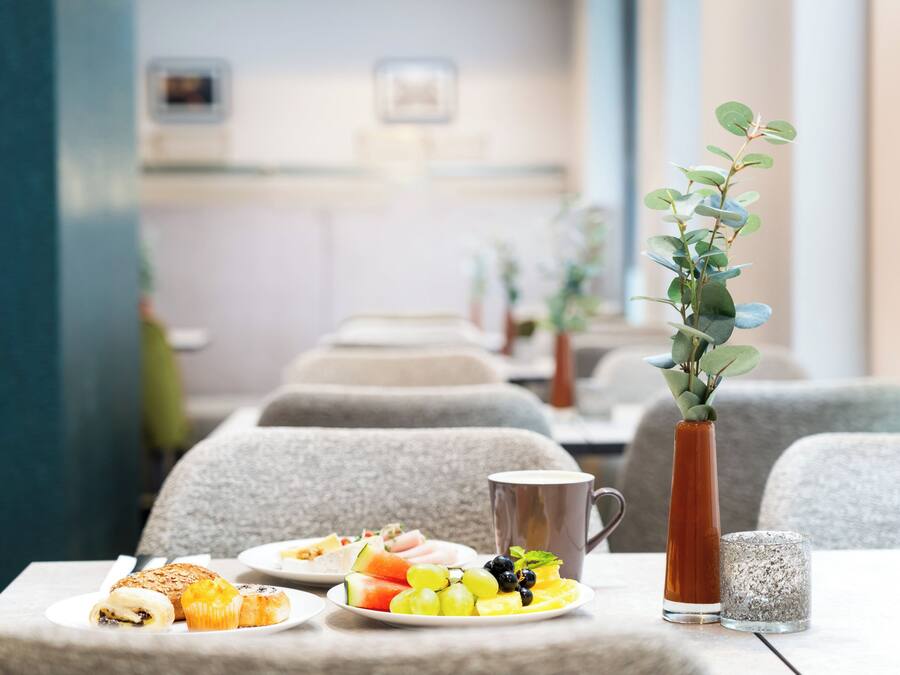 Uma mesa de café da manhã com pratos de doces, frutas e uma xícara de café.