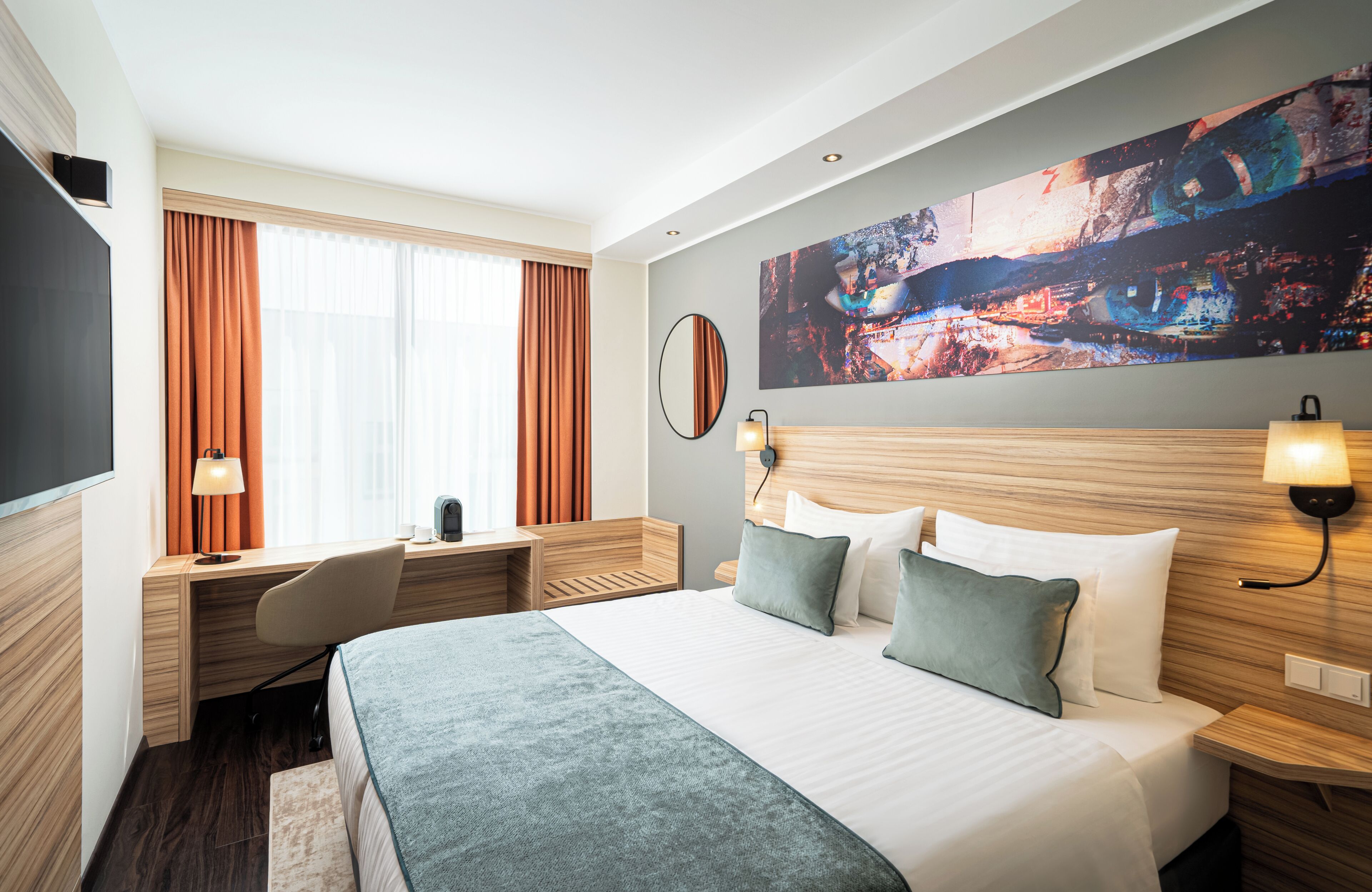Quarto de hotel com uma cama grande, uma escrivaninha, uma cadeira, uma televisão e um quadro na parede.