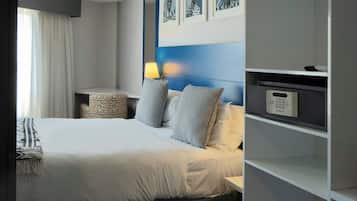 Quarto de hotel com cama, mesas de cabeceira, abajur, prateleira com um controle remoto e quadro na parede.