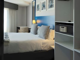 Quarto de hotel com cama, mesas de cabeceira, abajur, prateleira com um controle remoto e quadro na parede.