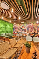 Quarto com parede verde, móveis de fibra natural e um mural geométrico colorido.