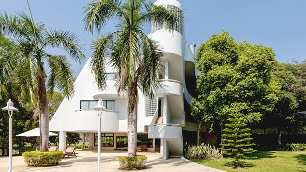 Um edifício moderno com design arquitetônico único, apresentando uma torre cilíndrica, um telhado plano e uma grande janela de vidro.