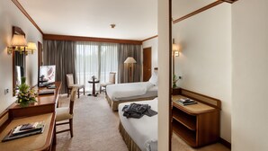 Quarto de hotel com duas camas, uma escrivaninha com cadeira, televisão e um espelho grande.