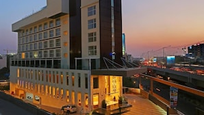 Um hotel moderno com vários andares, um terraço no topo e vista para a paisagem urbana ao entardecer.