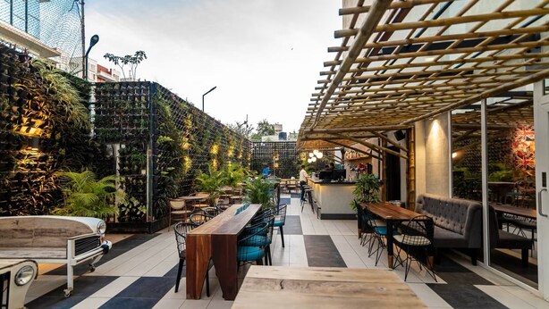 Restaurante com design moderno, que oferece uma combinação de mesas internas e externas, diversos tipos de plantas e uma estrutura de parede singular.