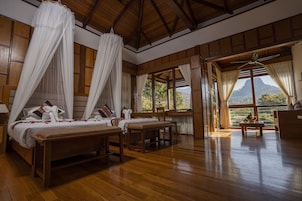 Um quarto com piso de madeira, cama com dossel, um banco e uma mesa.
