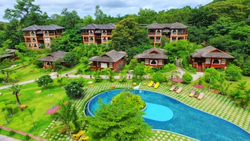 Resort com várias cabanas de madeira, uma piscina central e vegetação exuberante.