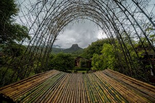 Estrutura de bambu tradicional com vista para uma montanha e vegetação exuberante ao fundo.