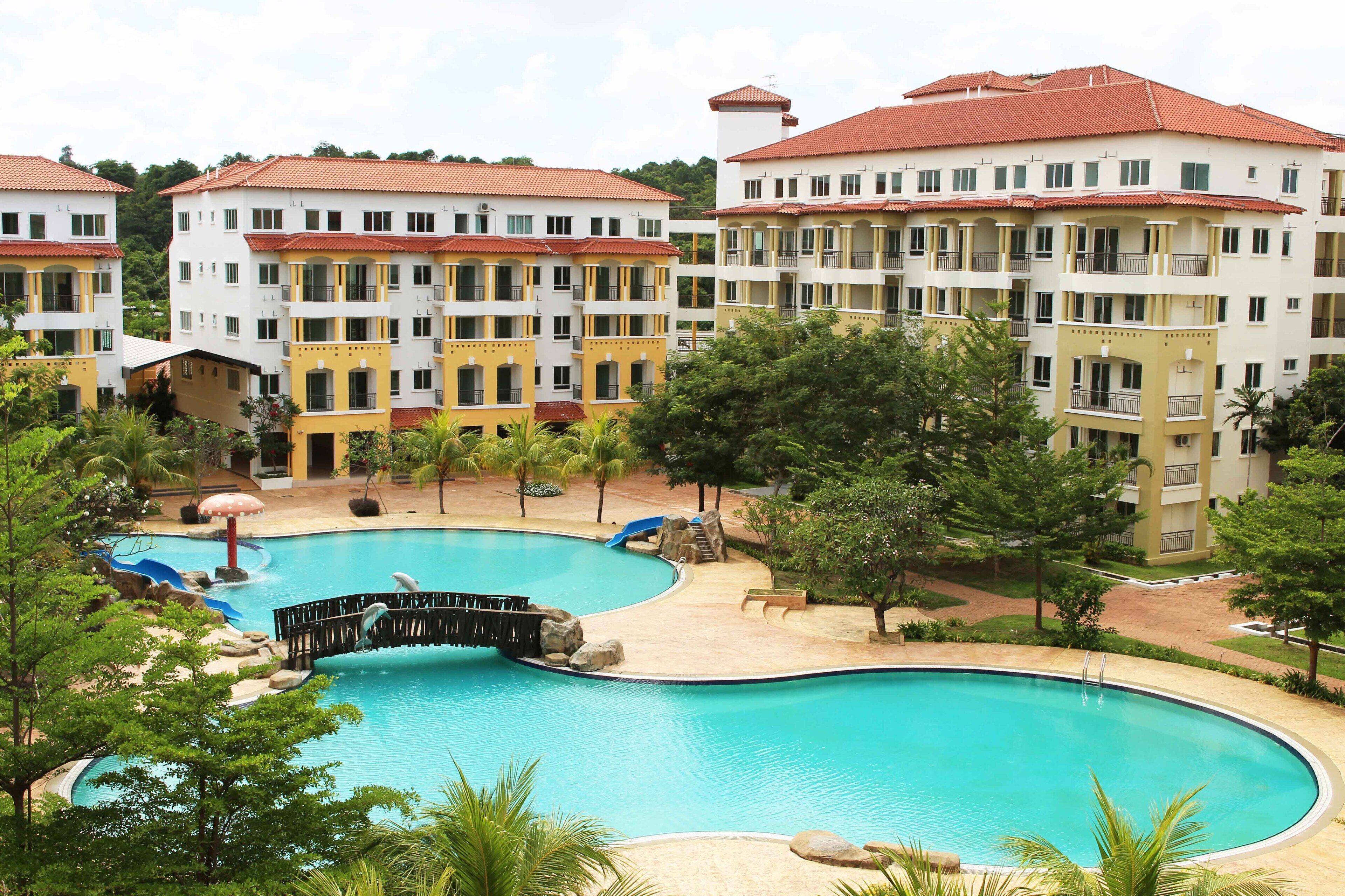 Um resort com uma grande piscina, vários edifícios com varandas e uma ponte sobre a piscina.