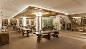 Uma sala de jantar espaçosa com uma grande mesa de madeira, várias mesas e cadeiras. Há uma escada com corrimão de madeira no lado direito.