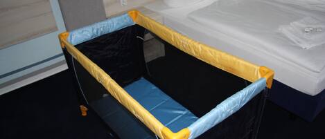 Uma cama com protetor de colchão e um berço portátil pequeno, com laterais amarelas e azuis.