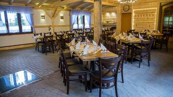 Um restaurante com várias mesas e cadeiras, vigas de madeira no teto e um relógio na parede.