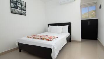 Quarto com cama, guarda-roupa preto, ar condicionado fixado na parede e janela com vista para uma montanha.