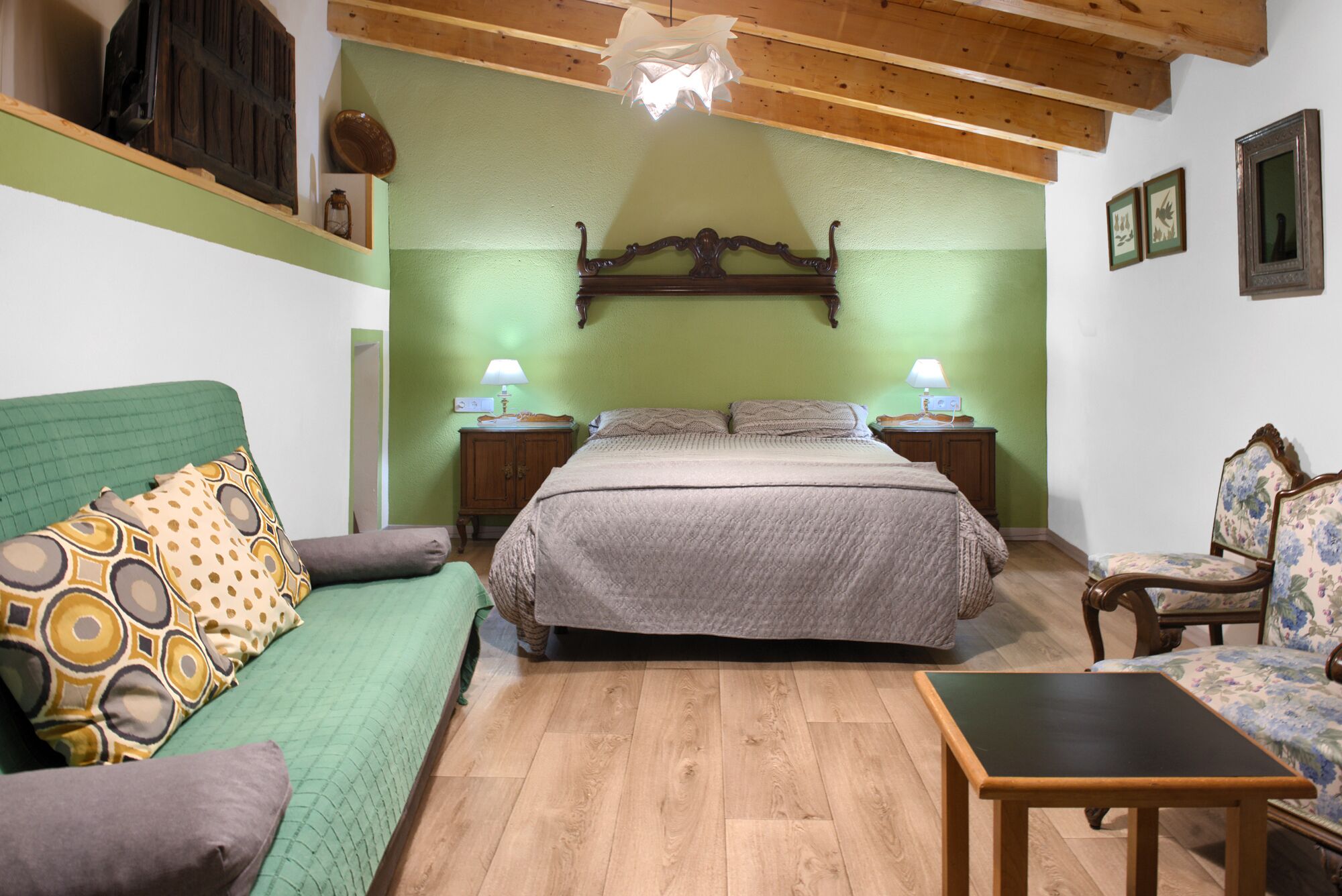 Um quarto com uma cama, um sofá verde, uma mesa de madeira e uma cadeira.