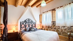 Quarto com teto de madeira, parede de pedra, cama com cabeceira, abajures e janela com cortinas.