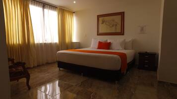 Quarto de hotel com uma cama, mesa de cabeceira, uma cadeira e um quadro na parede.