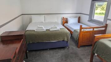 Quarto com duas camas de solteiro, cômoda de madeira, janela com vista para o verde e piso coberto por carpete.