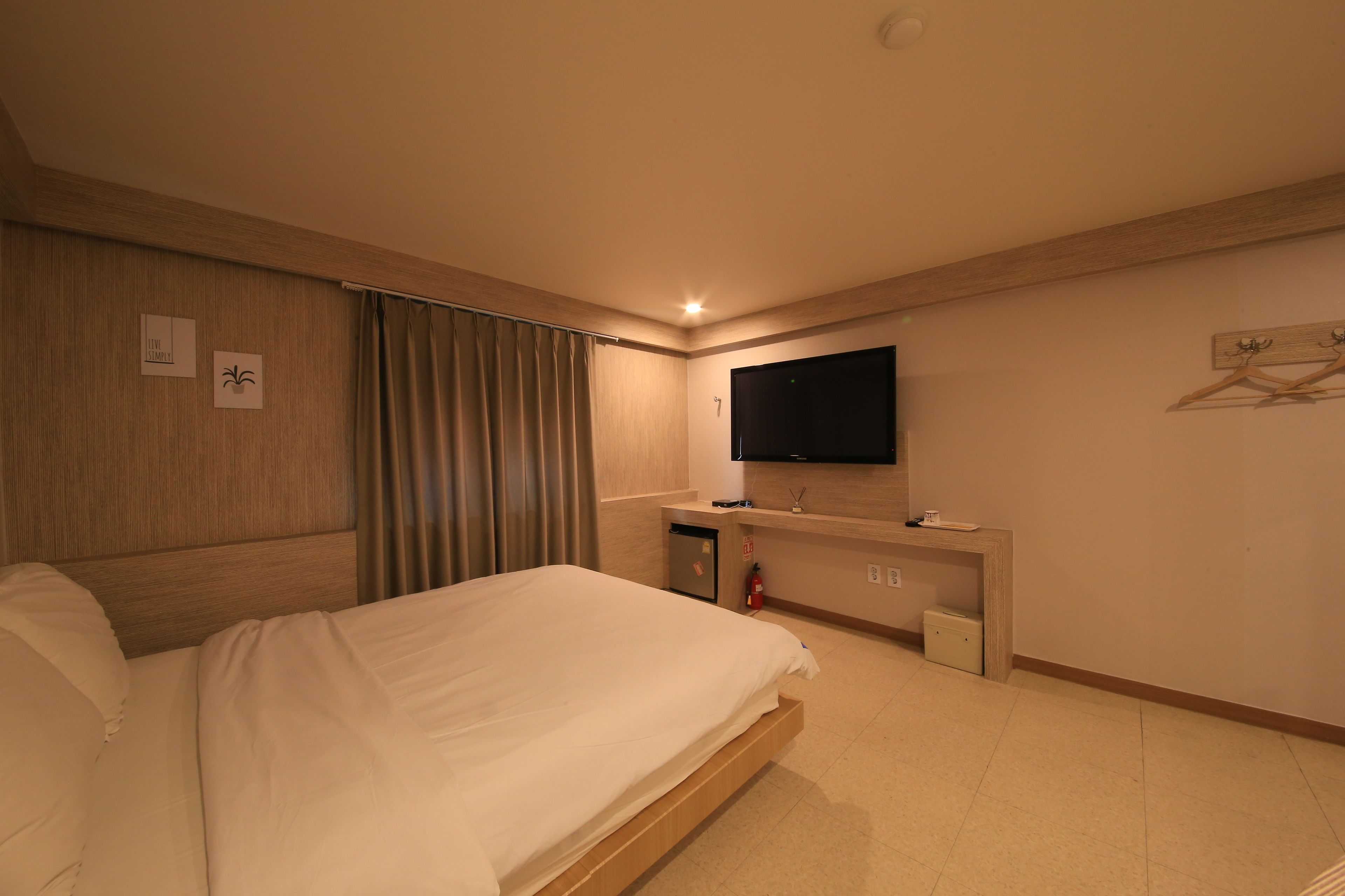 Quarto de hotel com cama, televisão, escrivaninha e extintor de incêndio.