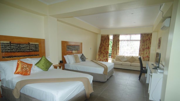 Quarto de hotel com duas camas, um sofá, uma mesa de trabalho e uma janela com cortinas.