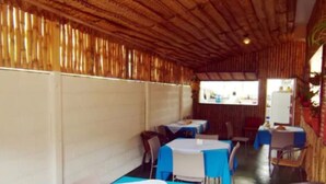 Restaurante com teto de bambu, mesas com toalhas azuis e brancas, e cadeiras.