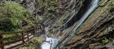 Uma ponte de madeira sobre um rio, com uma cascata à direita.