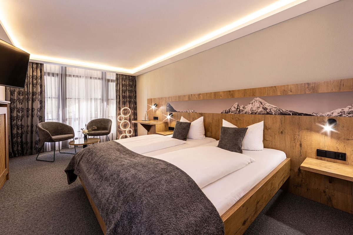Quarto de hotel moderno com uma cama grande, cabeceira de madeira, escrivaninha e uma cadeira.
