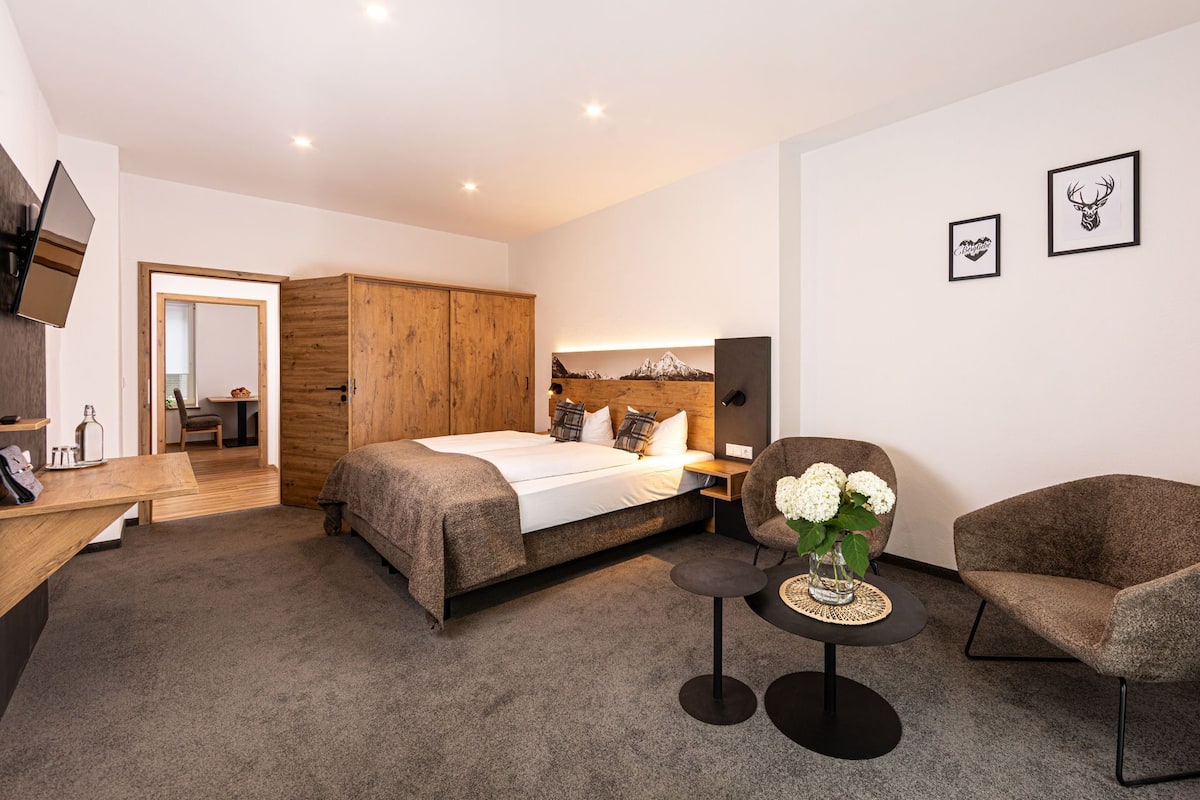 Quarto de hotel moderno com cama, armário de madeira, escrivaninha e cadeira. Há duas molduras com quadros na parede.