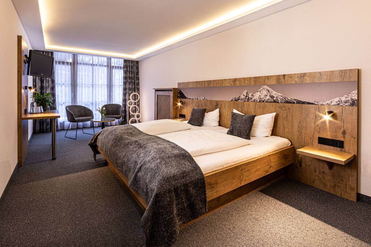 Quarto de hotel moderno com uma cama grande, uma escrivaninha com cadeira e uma televisão.