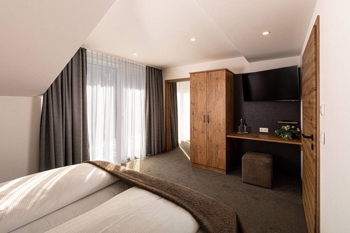 Quarto moderno com cama, guarda-roupa de madeira, televisão e um pequeno espaço para sentar.