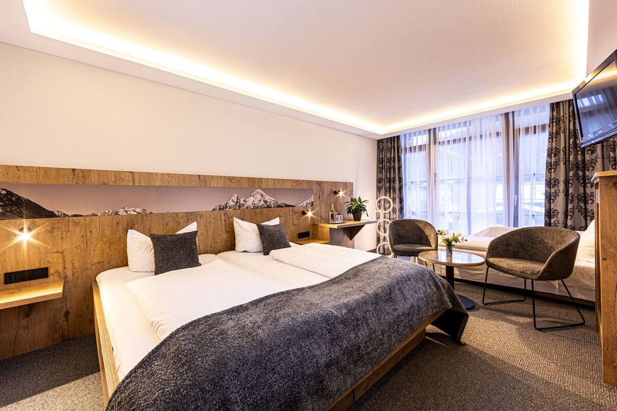 Quarto de hotel moderno com uma cama grande, uma escrivaninha, duas cadeiras e uma televisão.