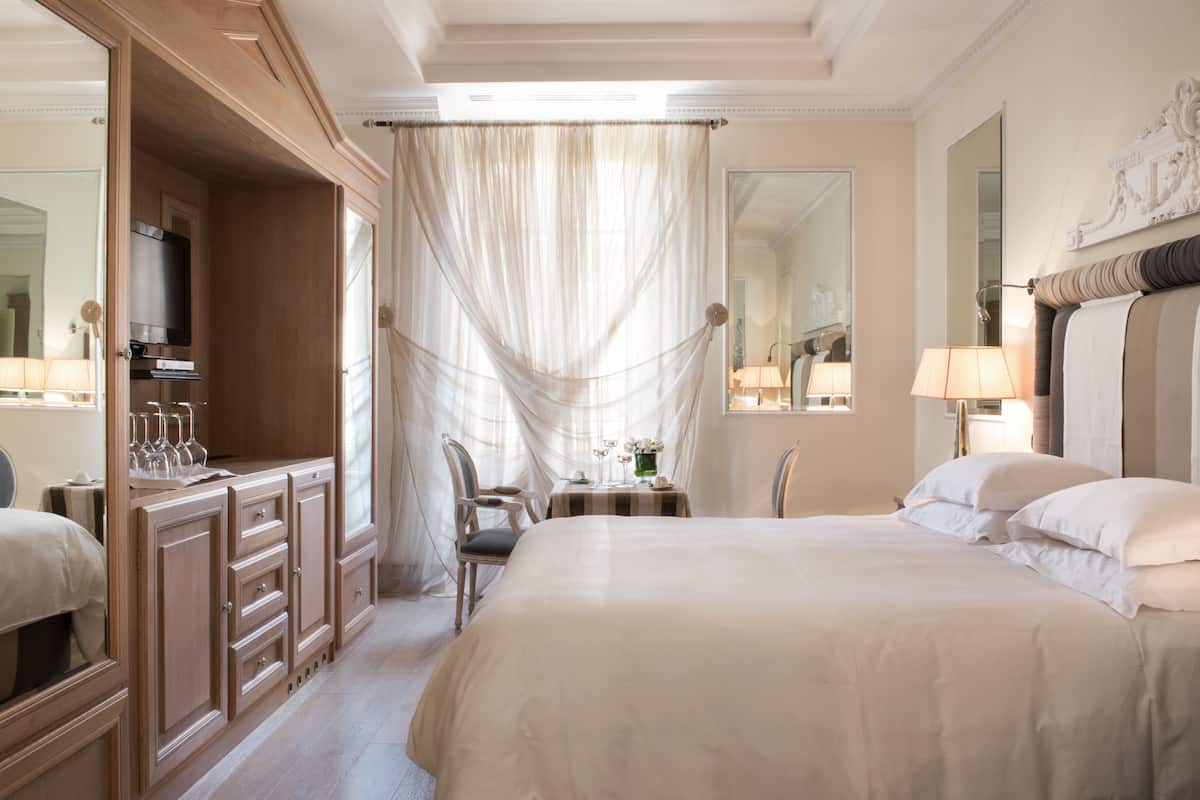 Quarto de hotel com uma cama grande, uma escrivaninha com candeeiro, uma cadeira e um guarda-roupa.