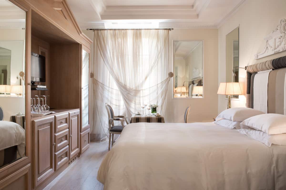 Quarto de hotel com uma cama grande, uma mesa com cadeira, televisão e guarda-roupa.